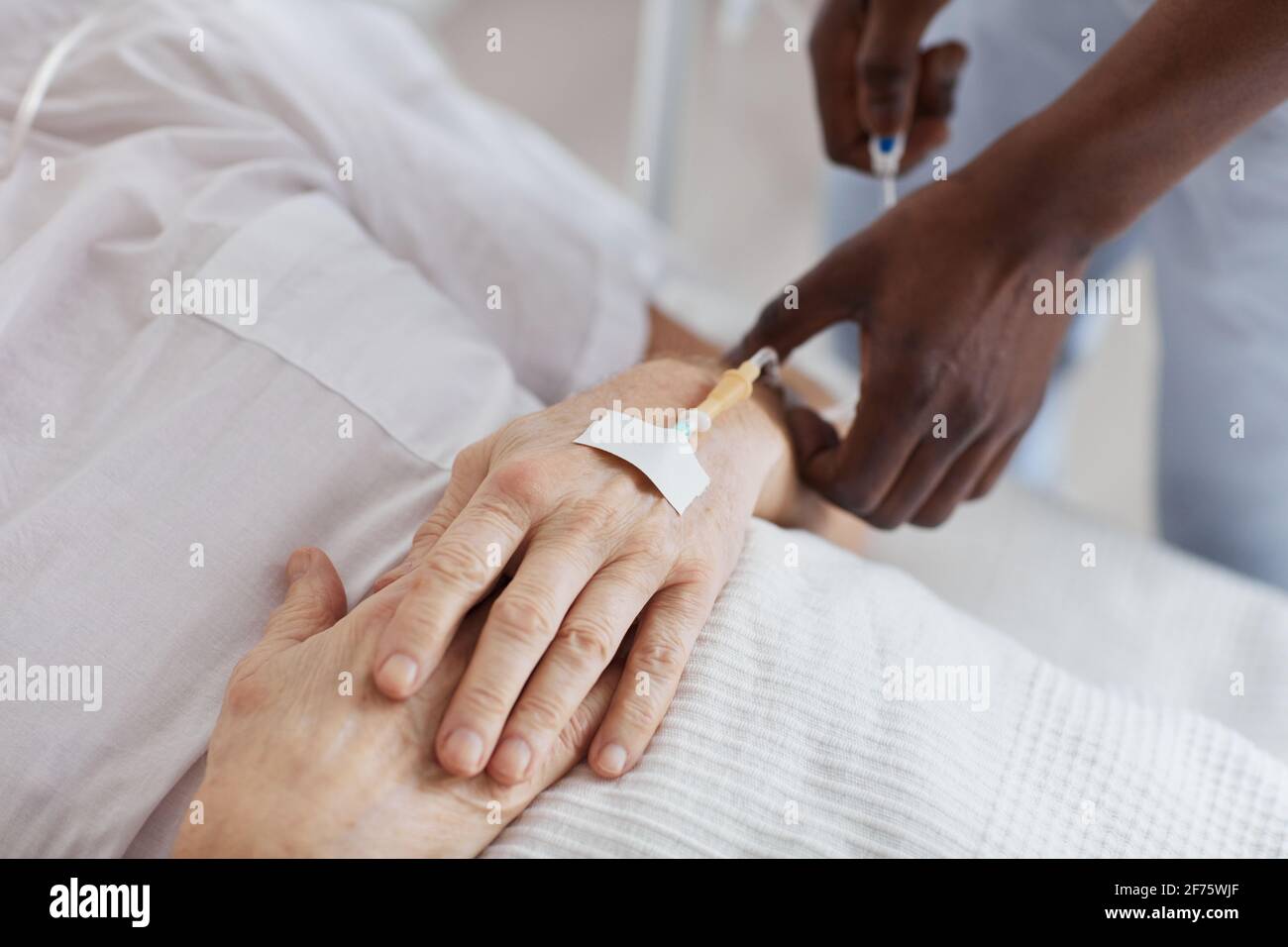 Close up of African-American male nurse setting up IV drip while caring ...