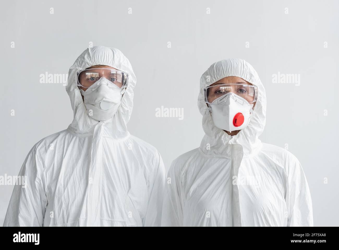 Scientists in hazmat suits and masks looking at camera isolated on grey ...