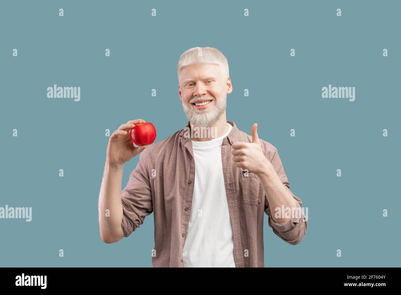 Healthy lifestyle. Happy young albino man holding red apple, gesturing ...