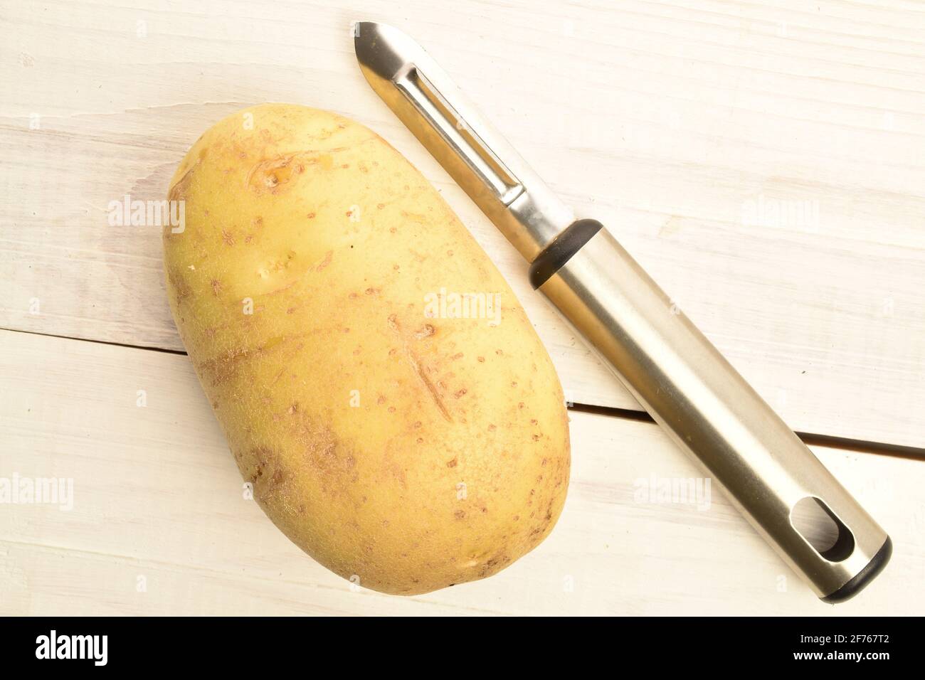 One fresh, not peeled, organic juicy, potato with a potato peeler, on a ...