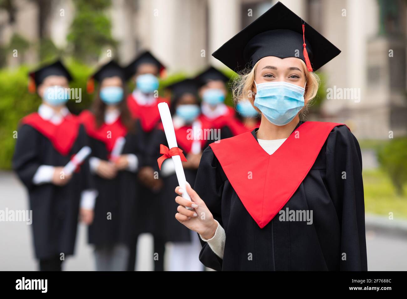 Lady student in graduation clothes showing diploma, wearing face mask ...