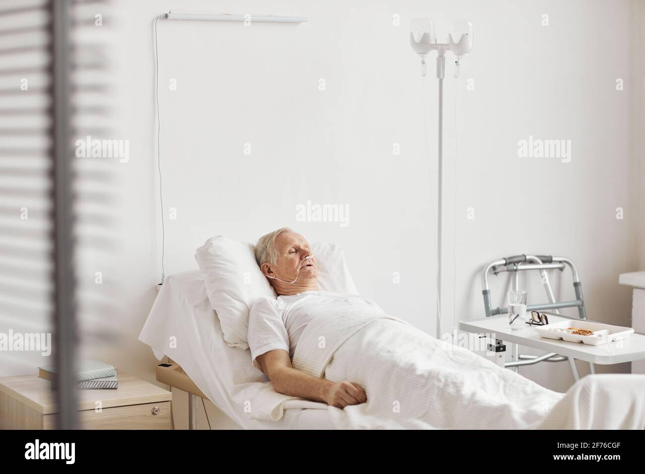 Portrait of senior man lying on bed in white hospital room with iv drip ...