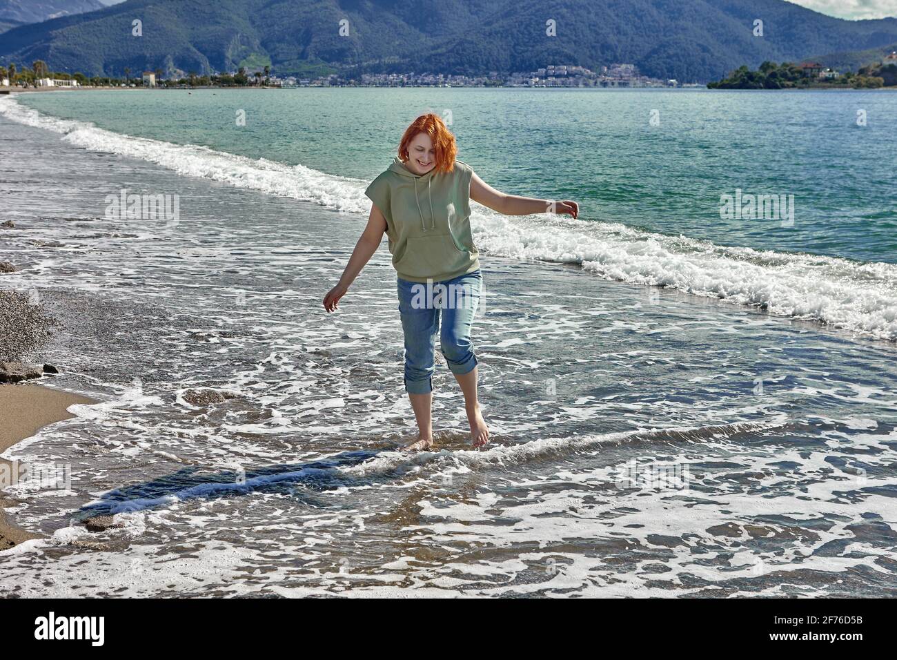 Young white woman walks barefoot on sand in surf line on beach in ...