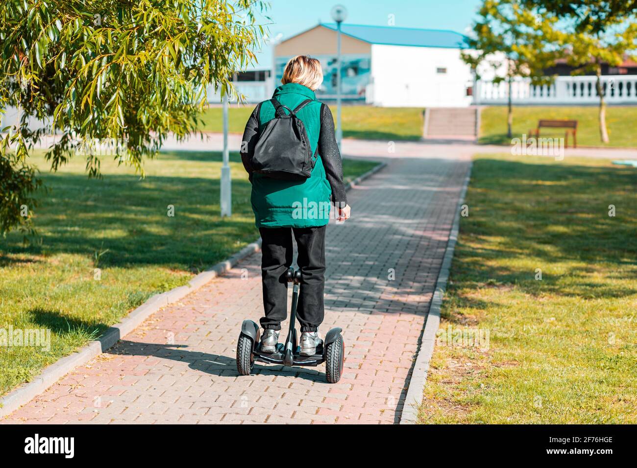An adult woman with a backpack on her back rides a Segway along a path ...