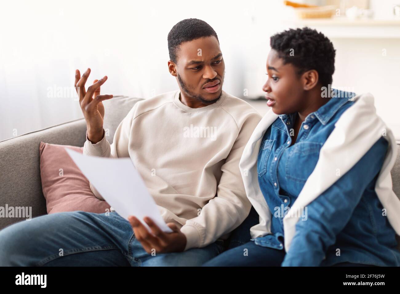 Confused afro couple reading documentation at home, sitting on sofa ...
