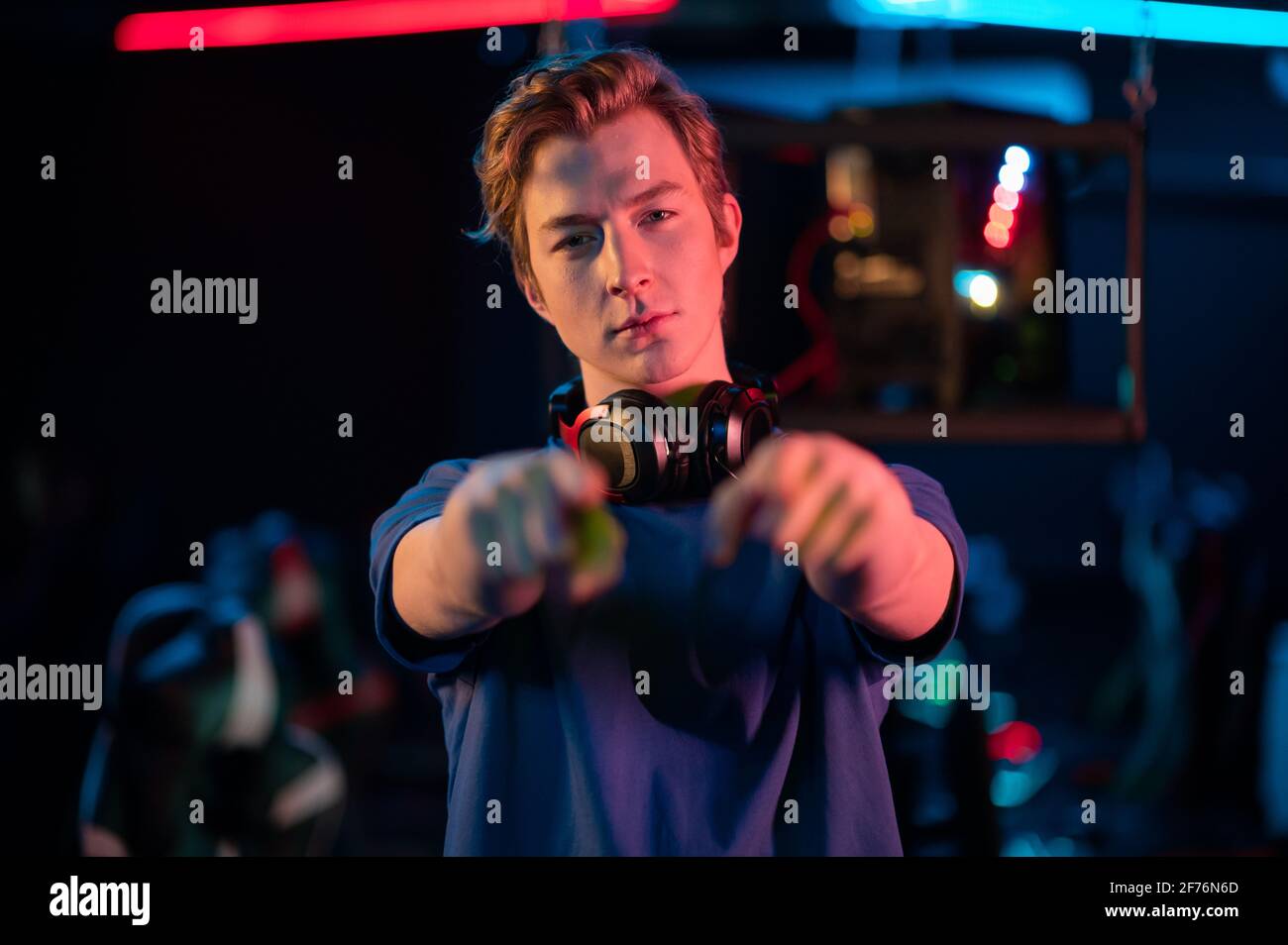 A cool gamer in a headset around his neck shows his hands to the camera ...