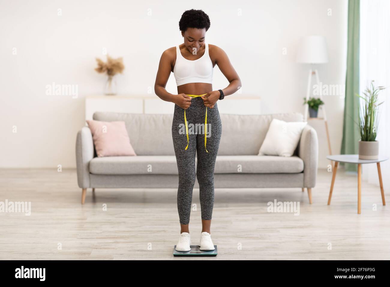 Joyful Black Female Measuring Waist Standing On Scales At Home Stock ...