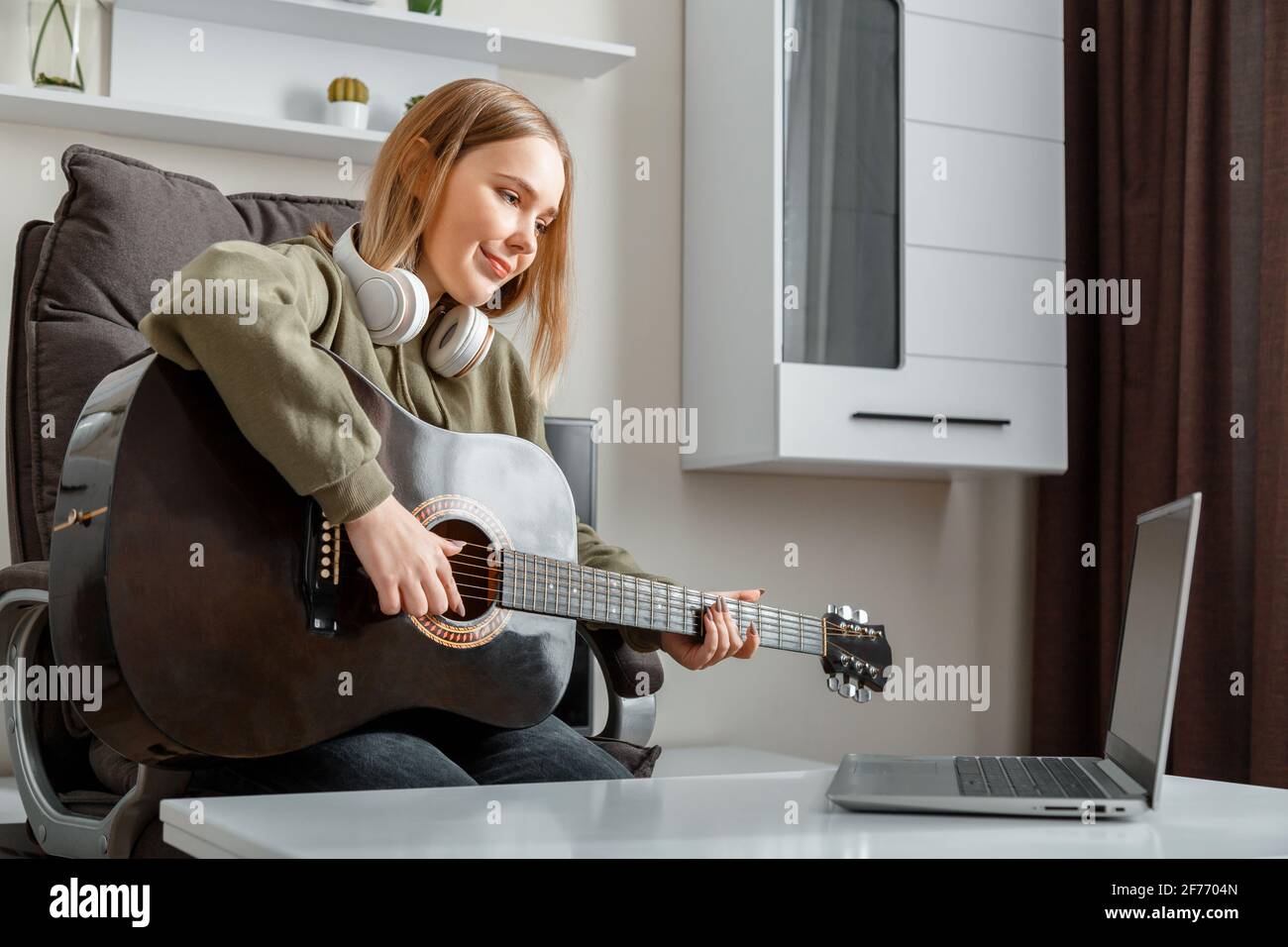 Teenager girl learning play guitar at home using online lessons. Hobby ...