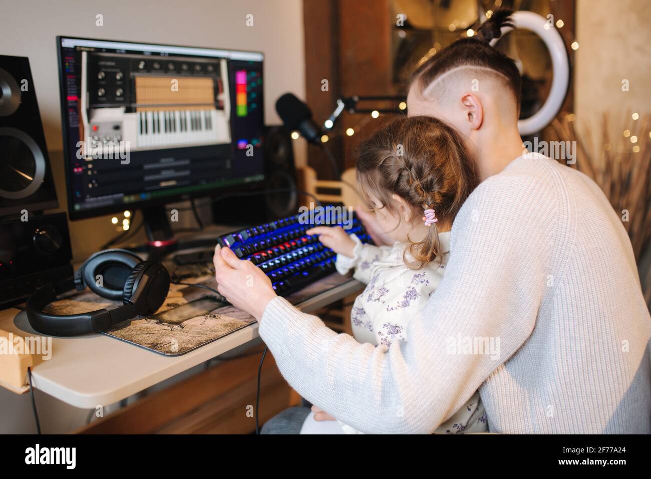 Younger sister sits on brothers knees and put finger on keyboard with ...