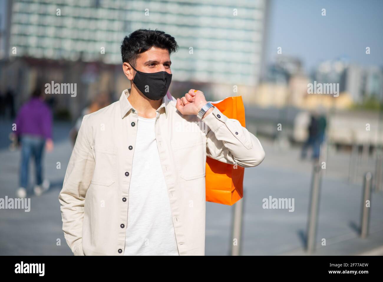 Masked young man carrying shopping bags while wearing a mask, covid and ...