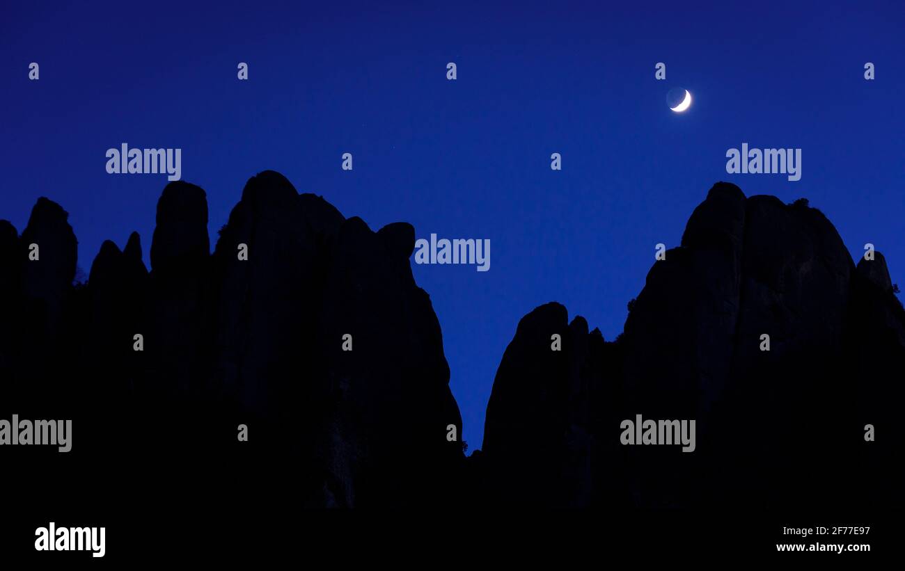 Crescent moon behind the silhouette of Montserrat spires at blue hour ...