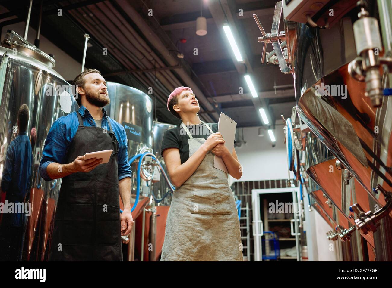 Two young successful workers of contemporary beer production factory ...