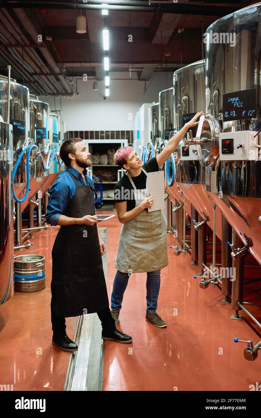 Two young workers of large beer production factory discussing new ...