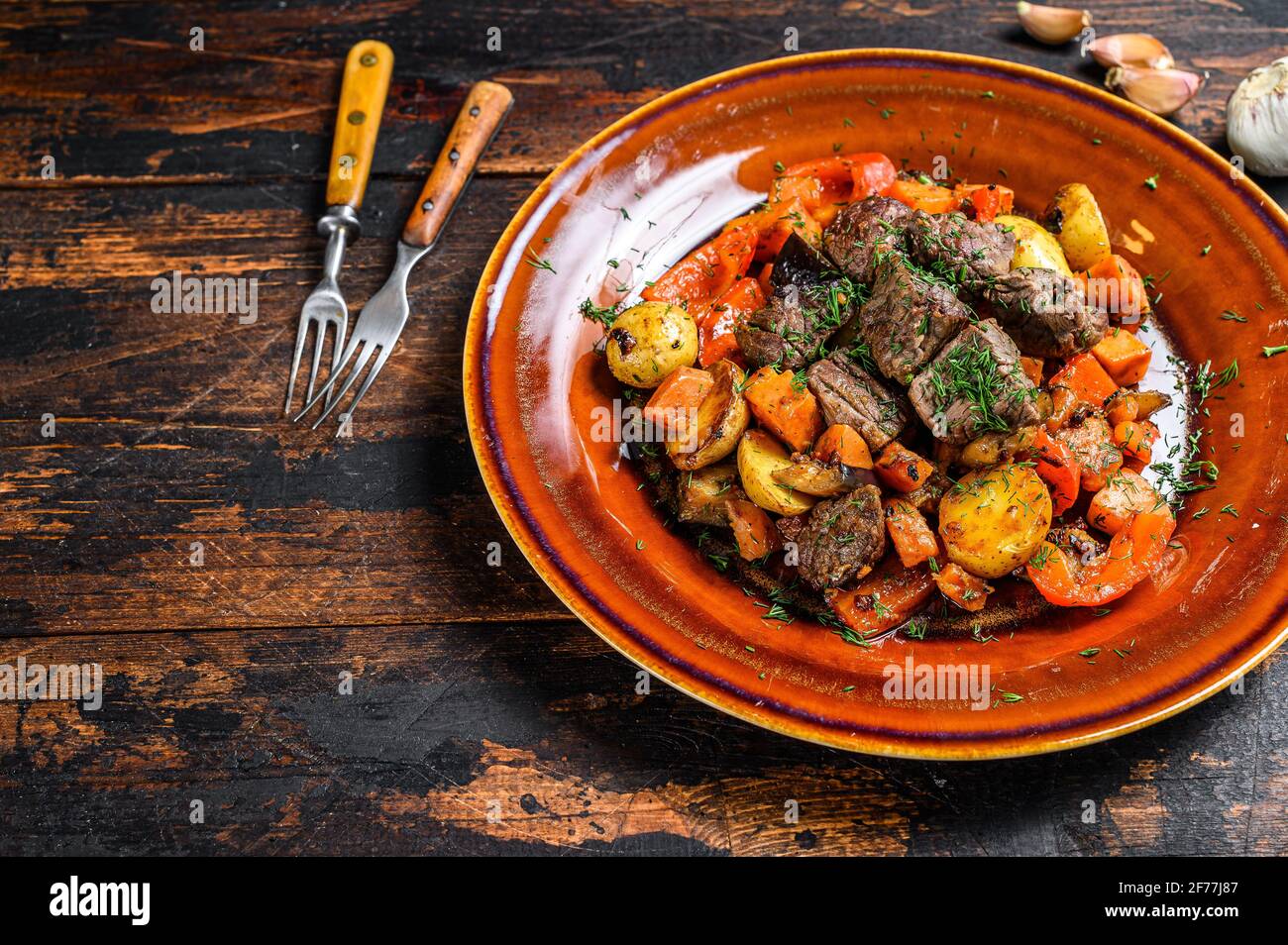 Beef meat stewed with vegetables on a plate. Dark wooden background ...