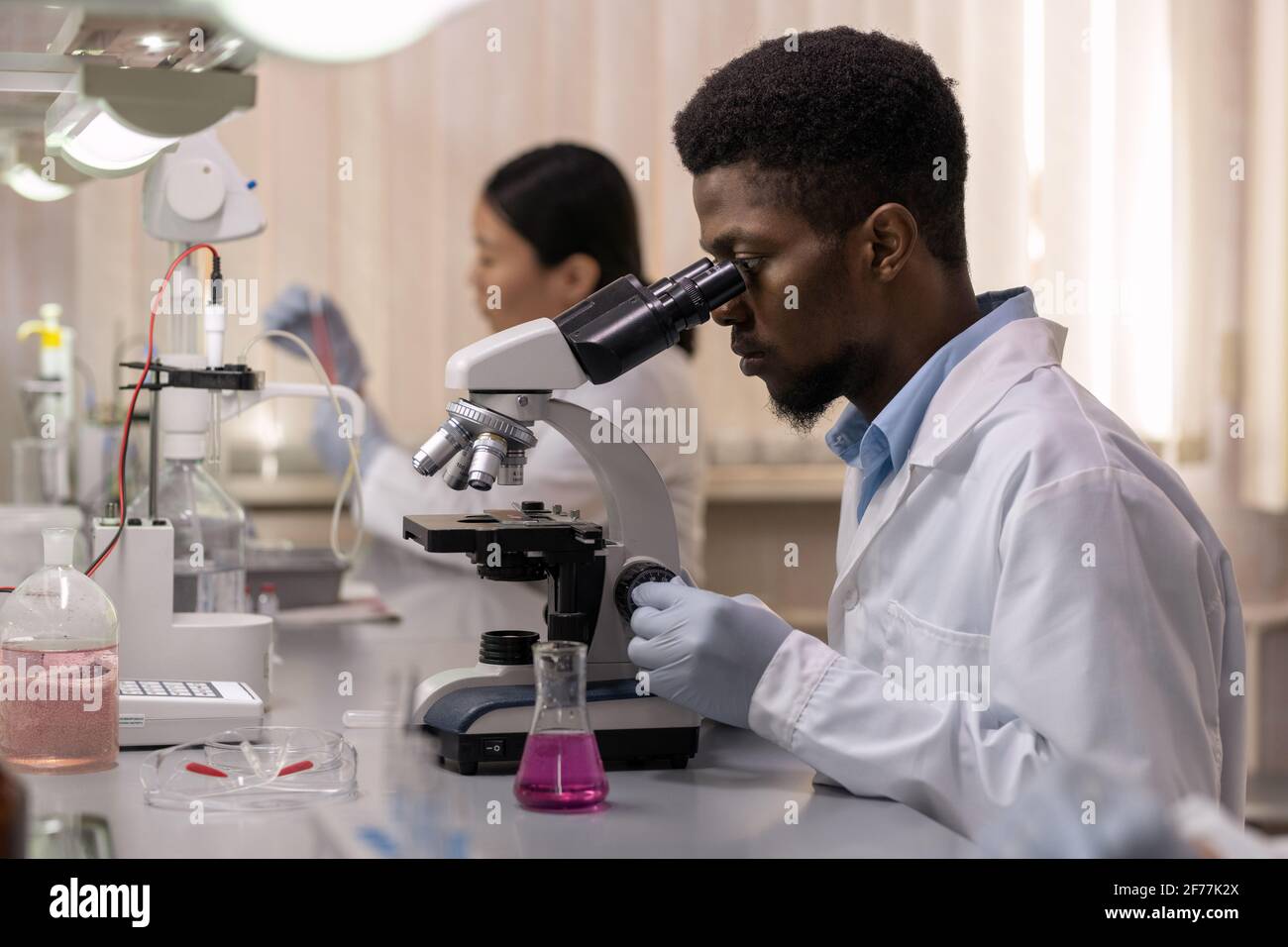 African young scientist sitting at the table looking through the ...