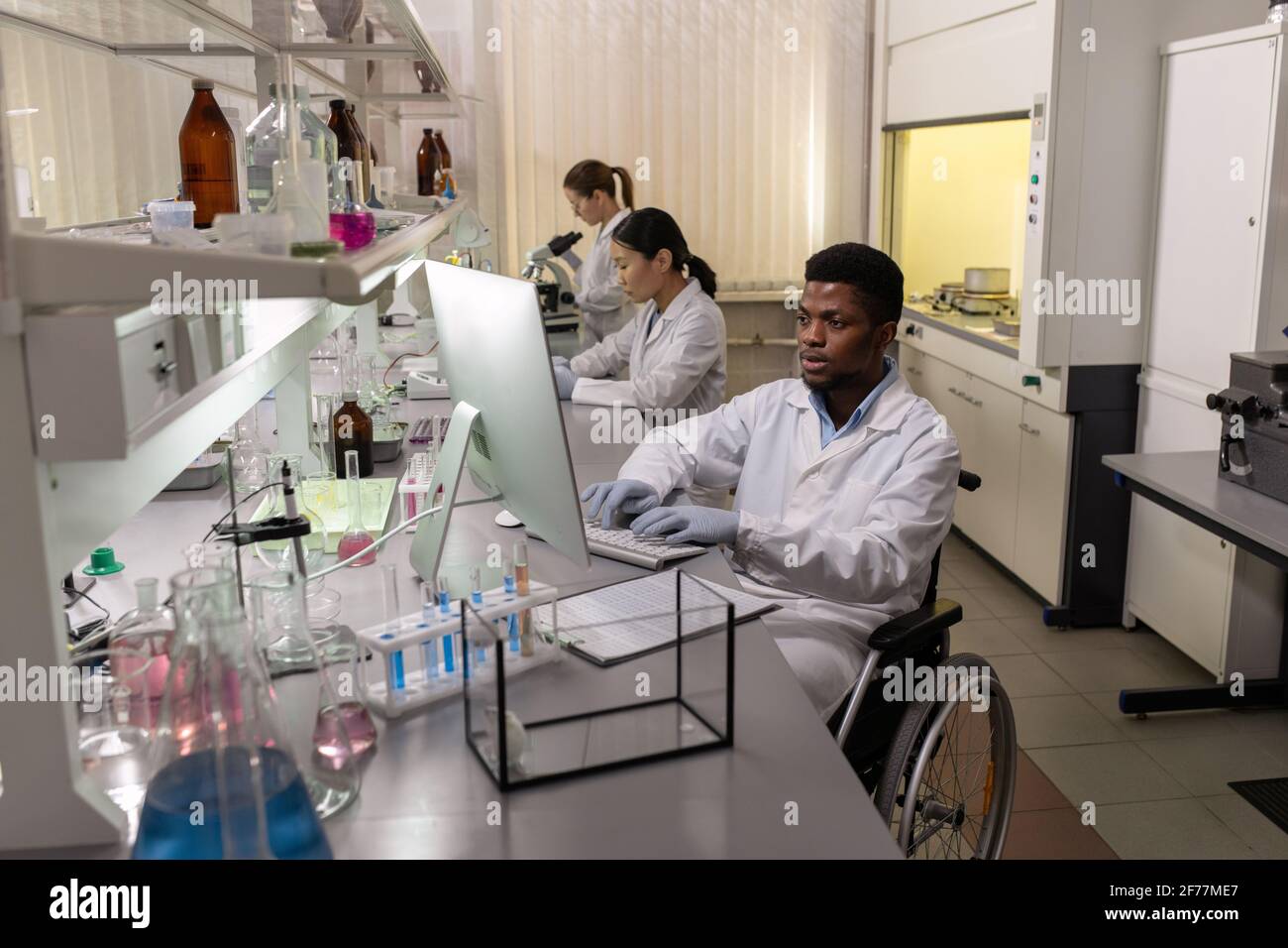 African disabled scientist sitting in wheelchair at the table and ...