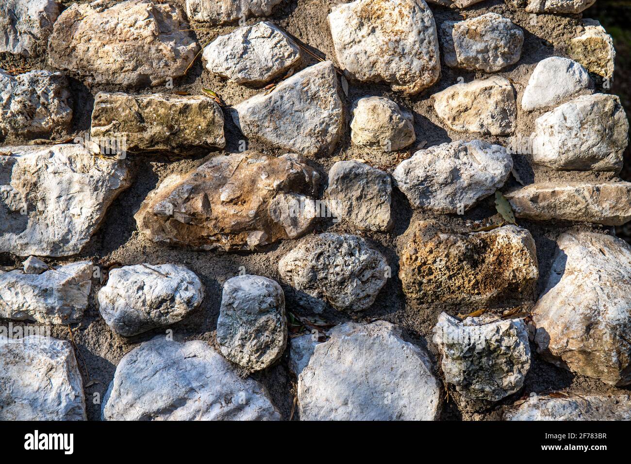 A portion of wall made of rough stones. The side sunlight highlights ...