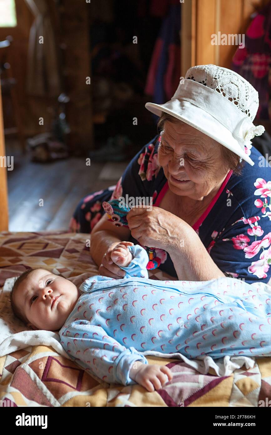 Happy senior granny looking at newborn grandchild lying on bed ...