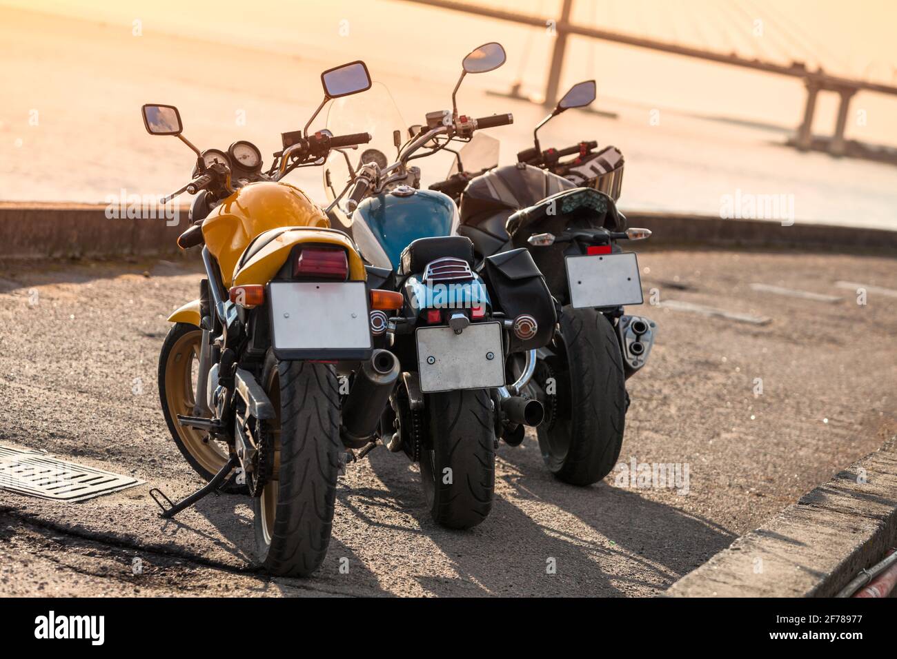 Three motorcycles standing in line on embankment under sun light ...