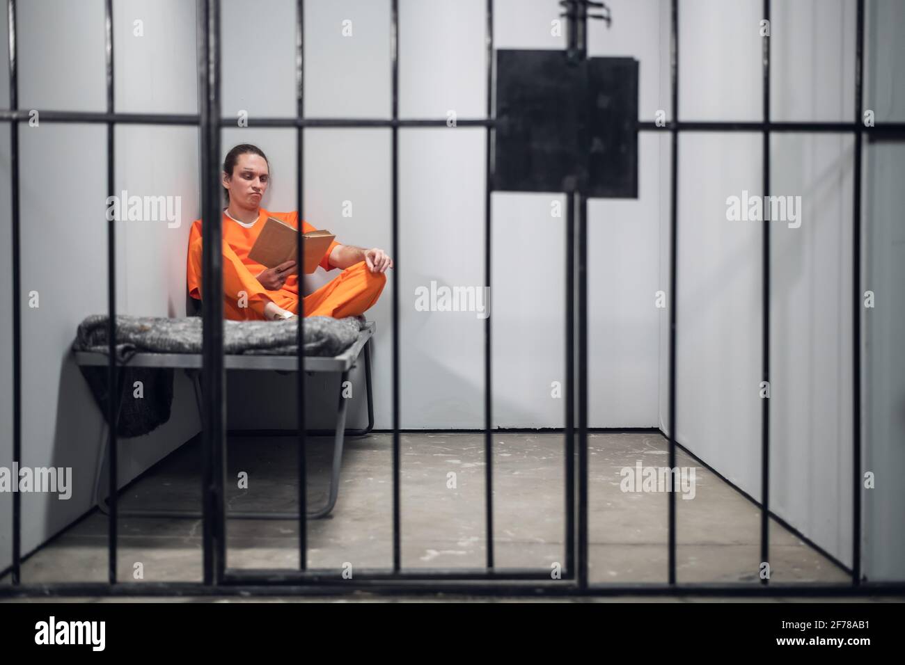A Latin young criminal in a solitary cell reads a book sitting on a ...
