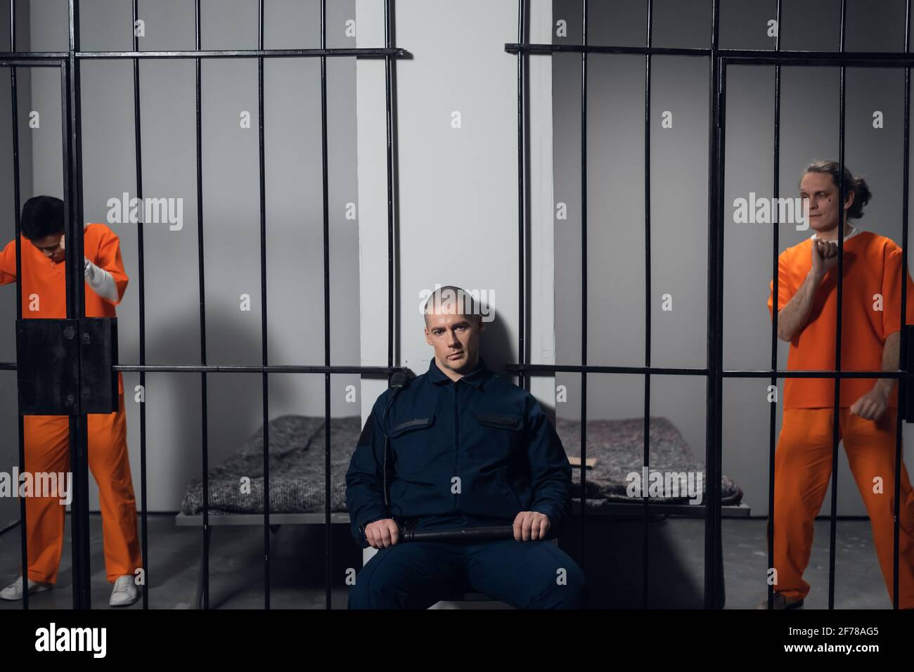 A strict prison guard in uniform guards cells with prisoners in a ...