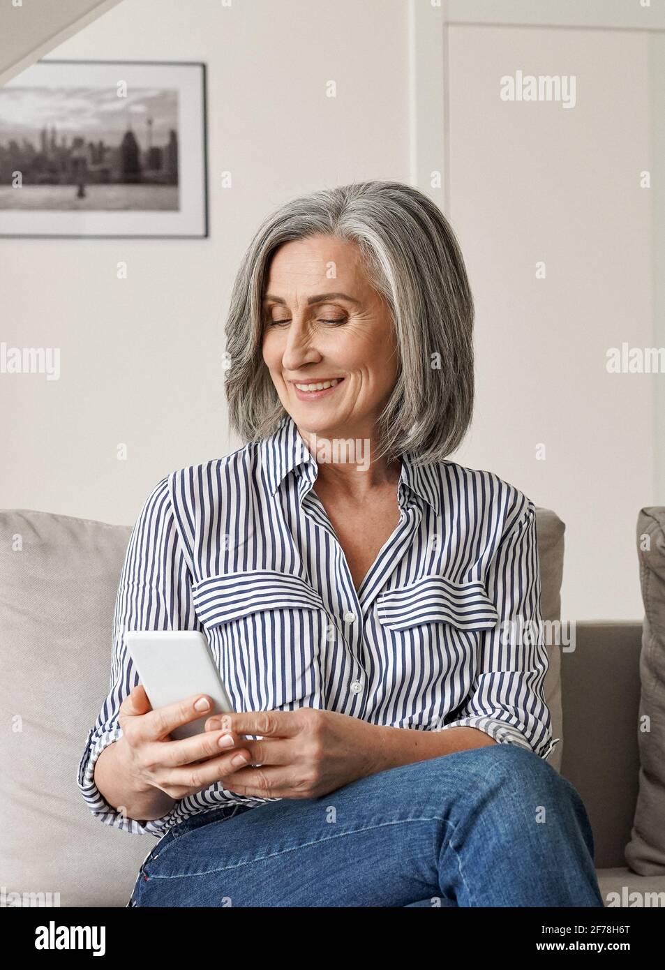 Happy older mature woman enjoying using cell phone sitting on couch at ... Happy older mature woman enjoying using cell phone sitting on couch at ...