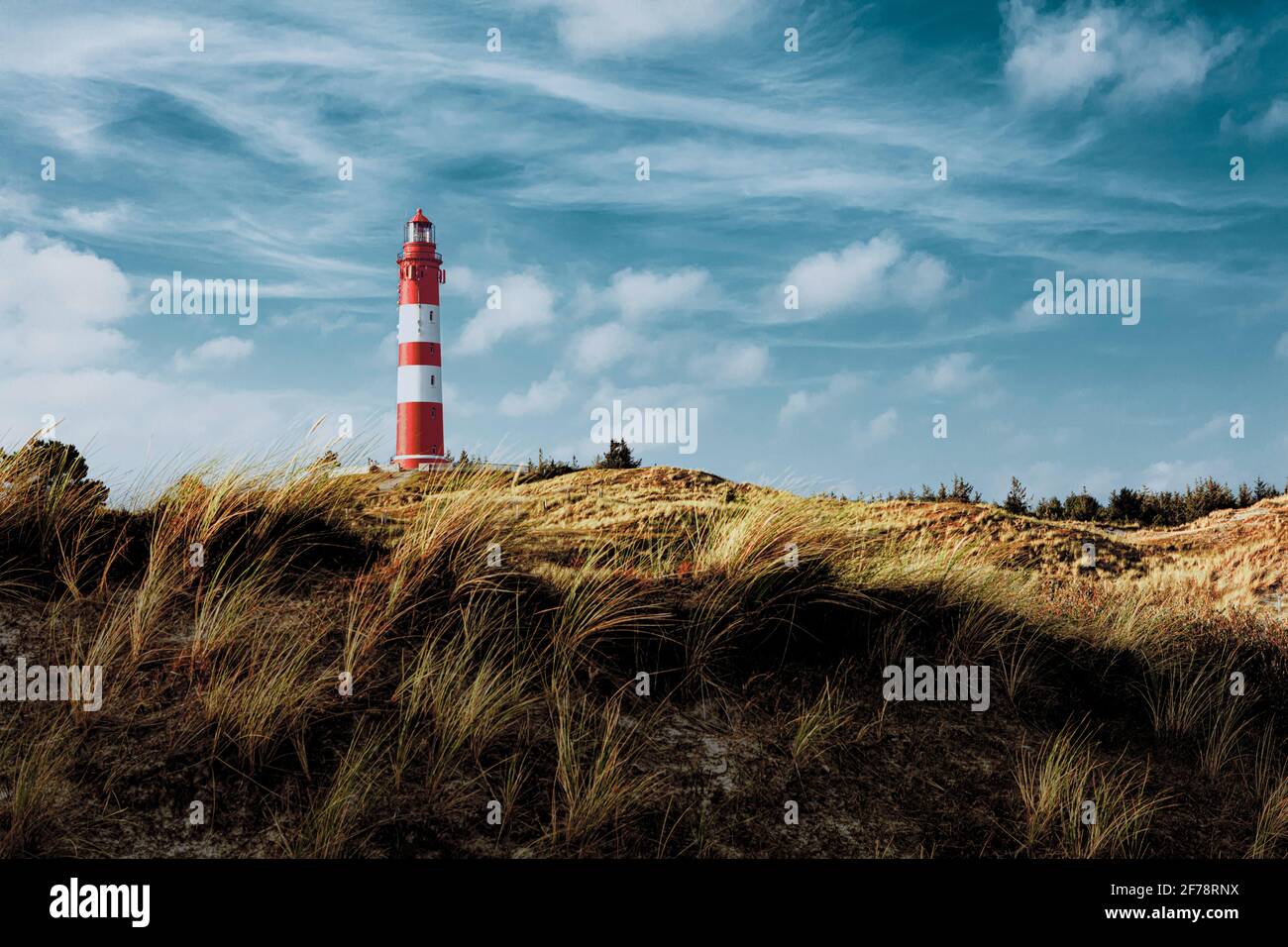 Tall red and white striped lighthouse on sand dunes in evening sunlight ...
