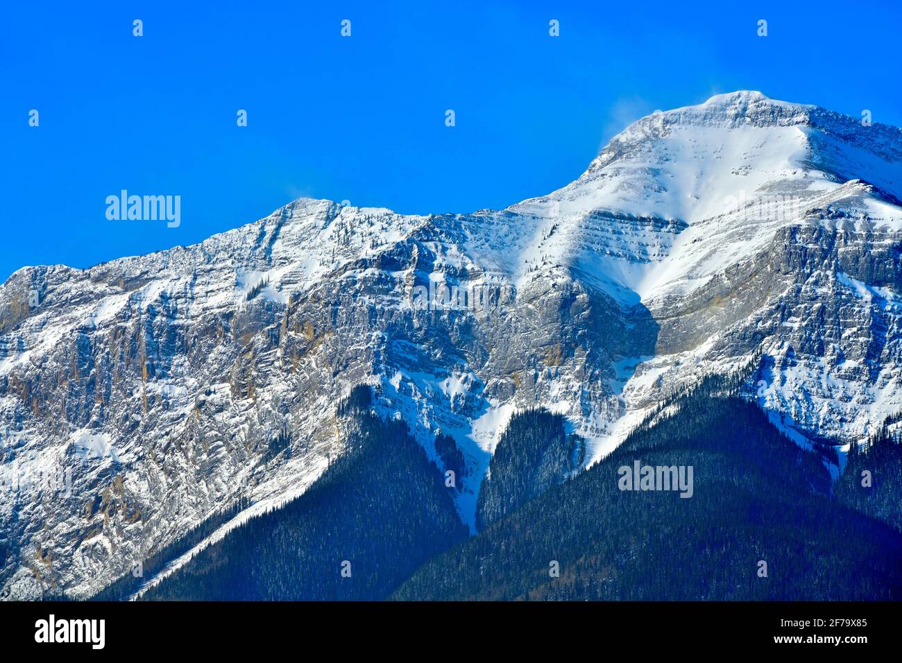 An image of a snow-capped rocky mountain peak with a bright blue sky in ...