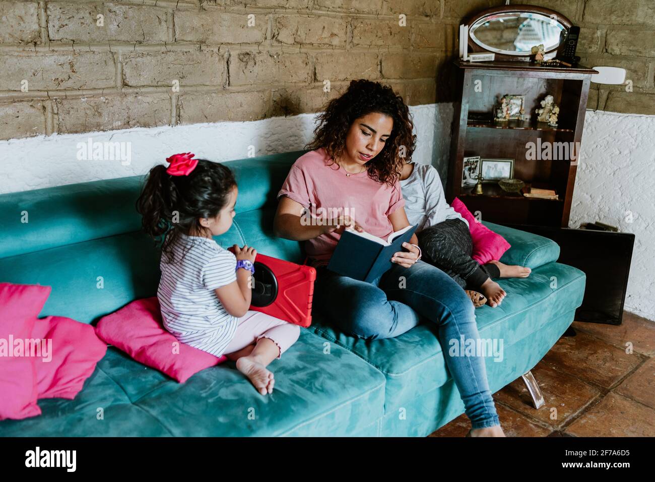 Young latin woman and her little children reading books at home in ...