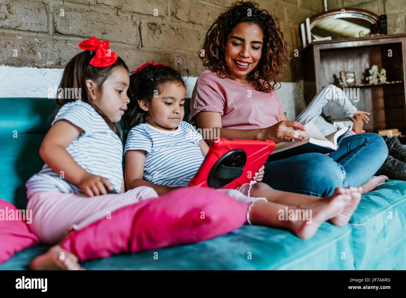 Young latin woman and her little children reading books at home in ...