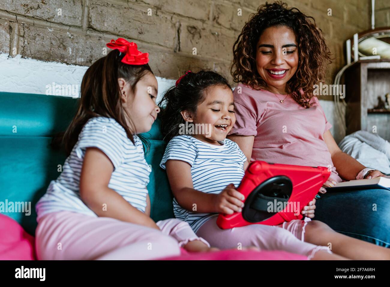 Young latin woman and her little children reading books at home in ...