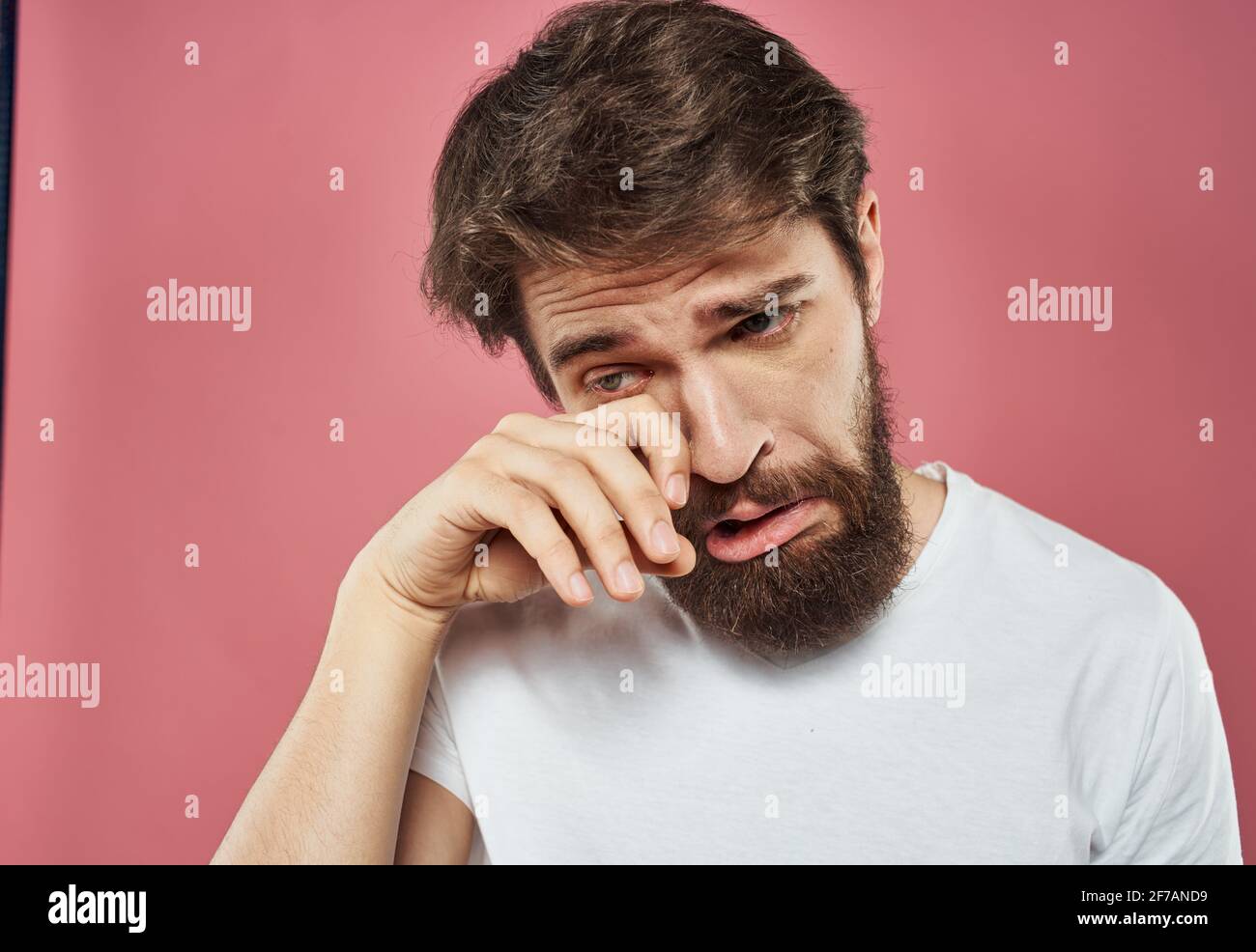Sad man crying on a pink background in a white t-shirt cropped view ...