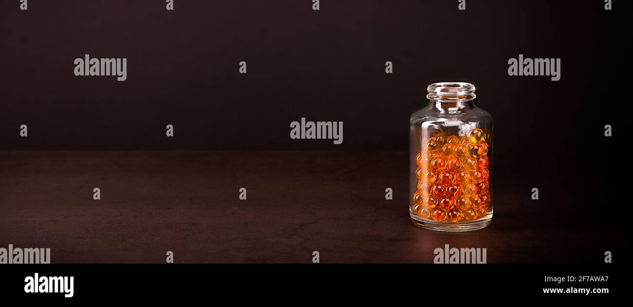 A glass jar with pills of bright orange yellow color on a brown ...