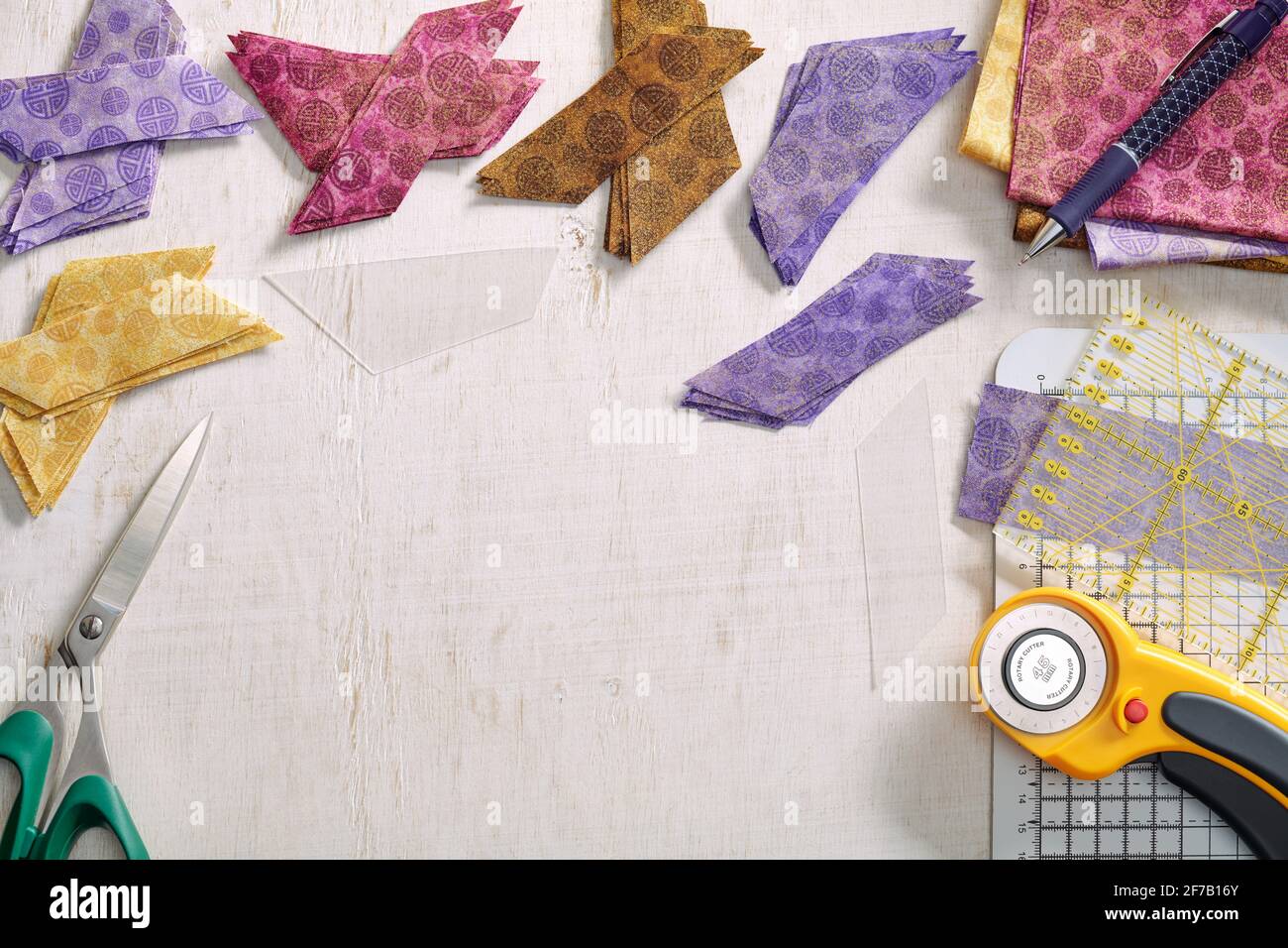 Stacks of multi-colored pieces of fabric, scissors, ruler, cutting mat ...