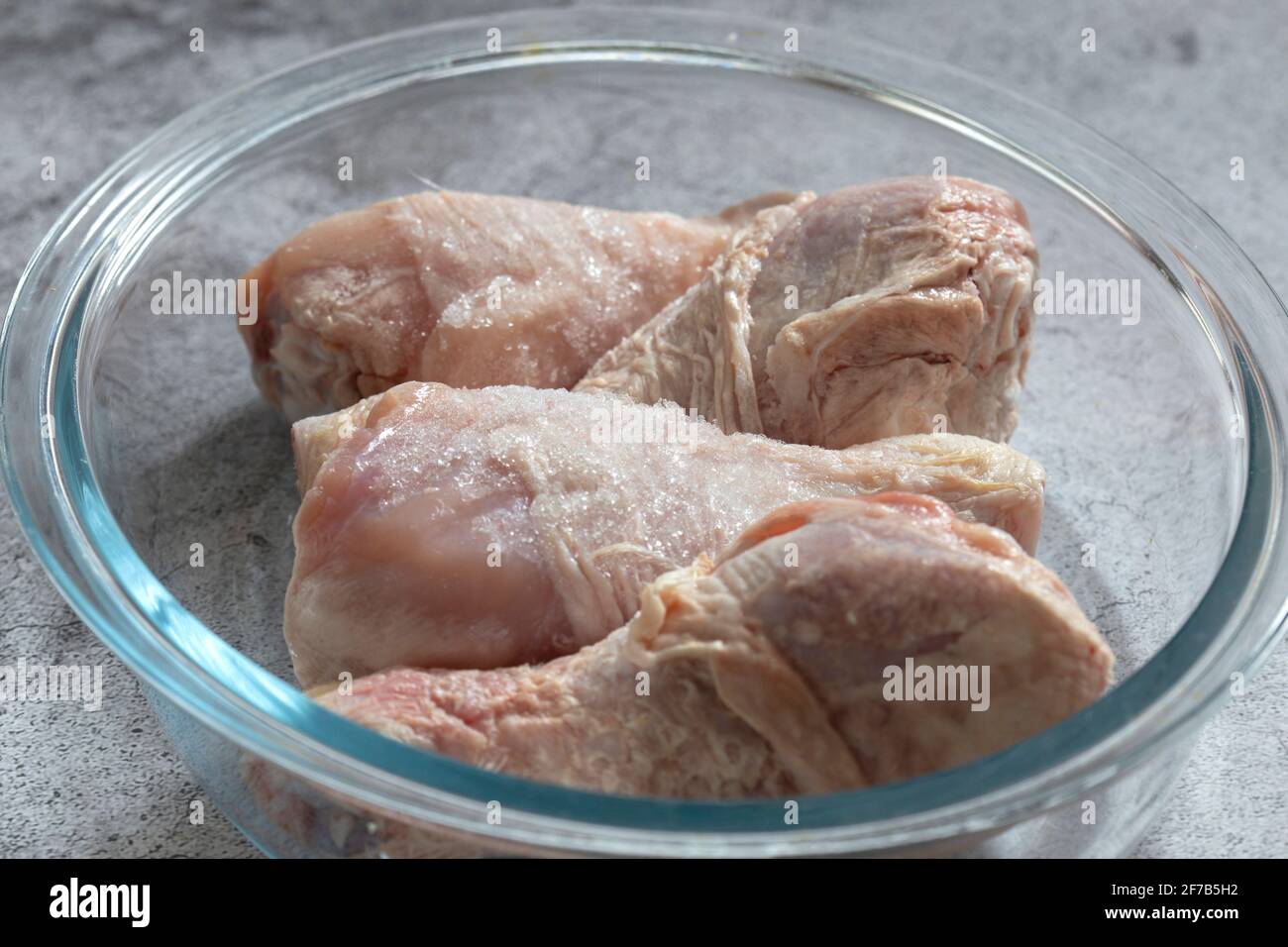 Frozen raw chicken defrosting in a glass dish. On a concrete background ...