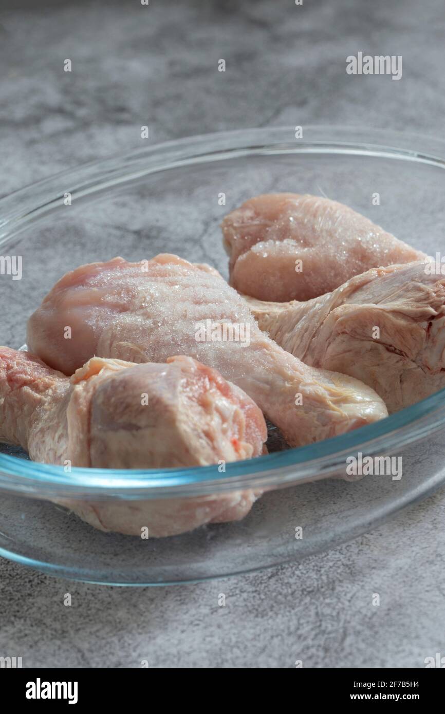 Frozen raw chicken defrosting in a glass dish. On a concrete background ...