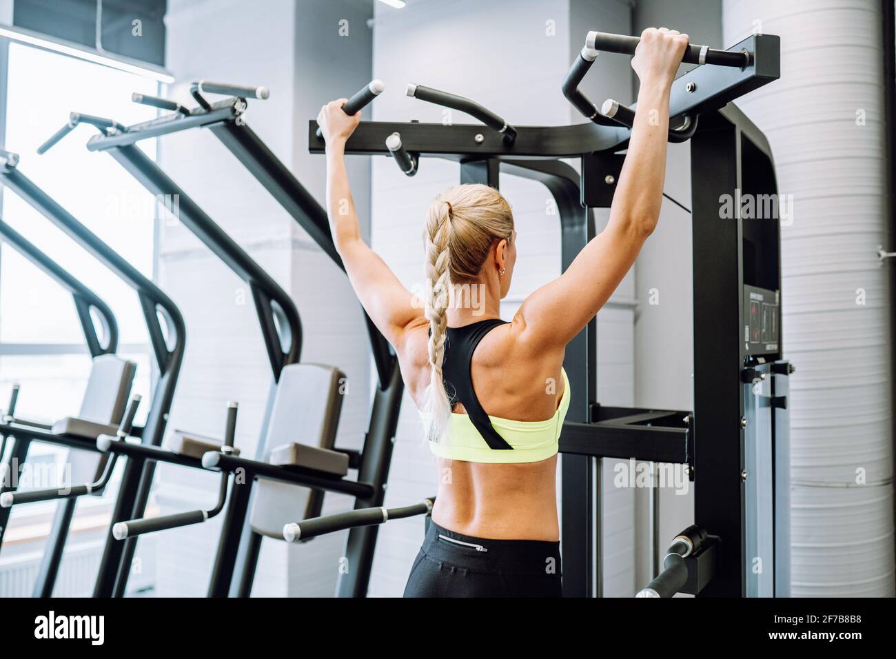 Blonde attractive slim woman wearing sport bra do exercises pull-ups on ...