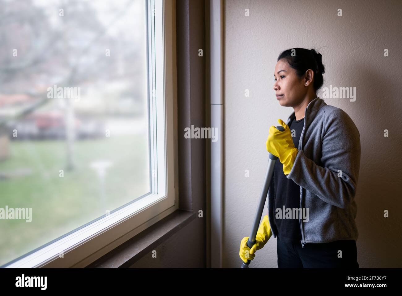 Woman holding mop and looking through window Stock Photo - Alamy