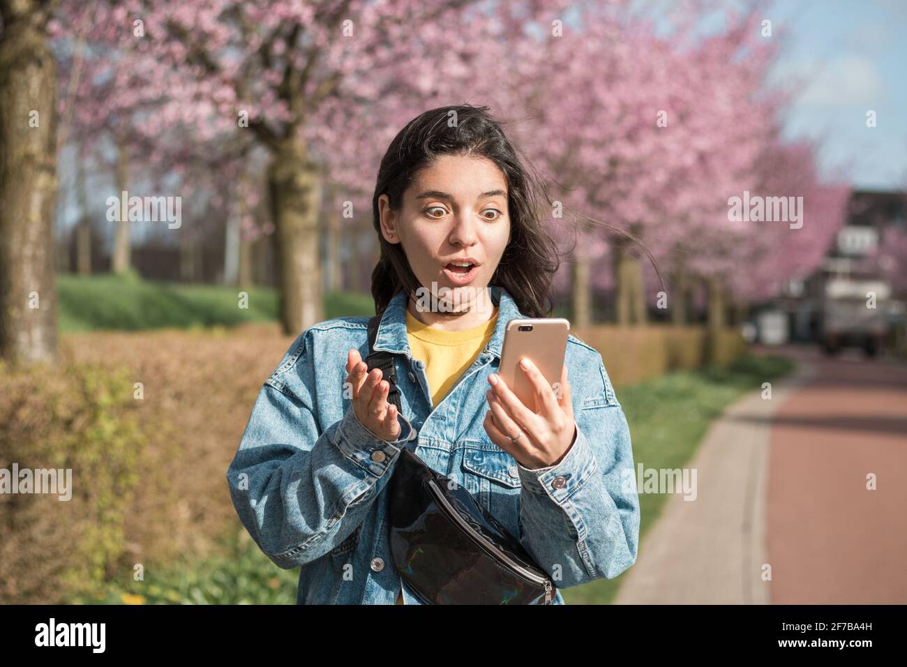shocked face expression of a mixed races woman looking into the phone while walking on the ...