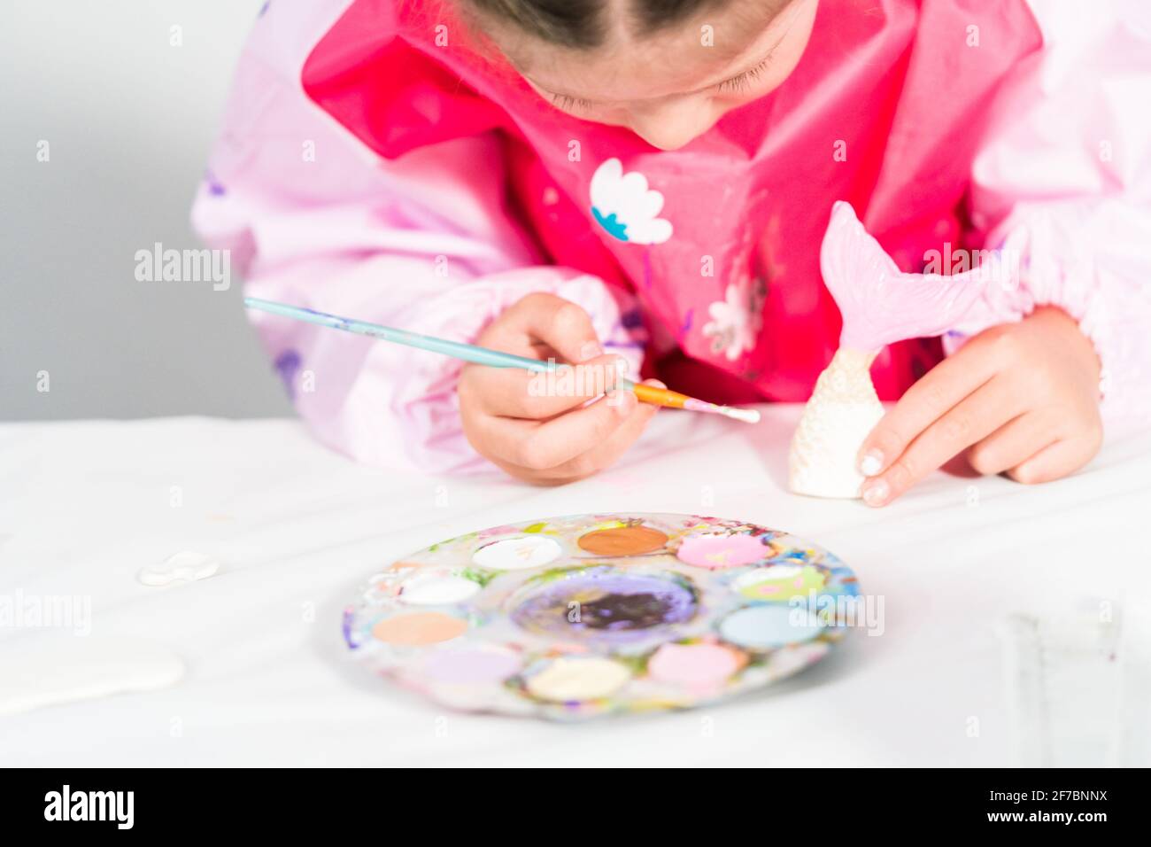 Little girl painting mermaid tails made out of modeling clay with ...
