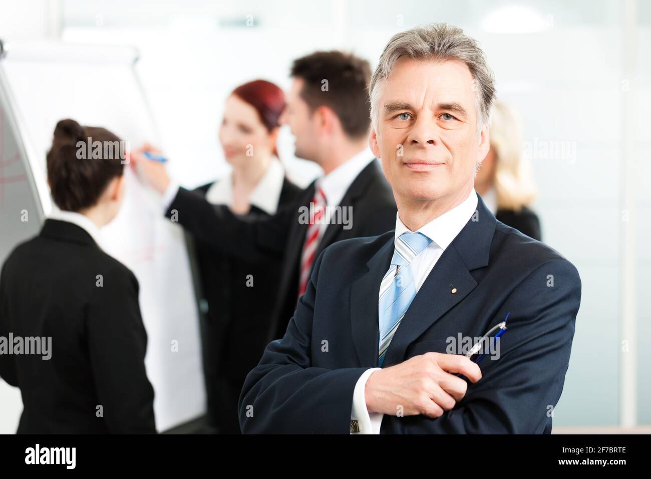 Business - team in an office, the senior executive is standing in front ...