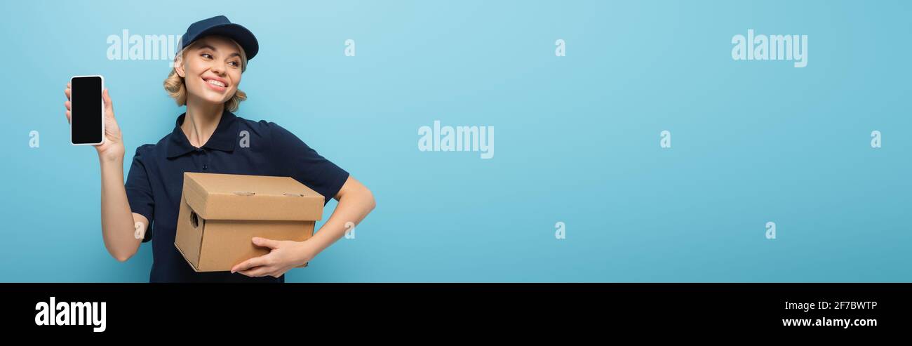 joyful courier showing smartphone with blank screen while holding ...