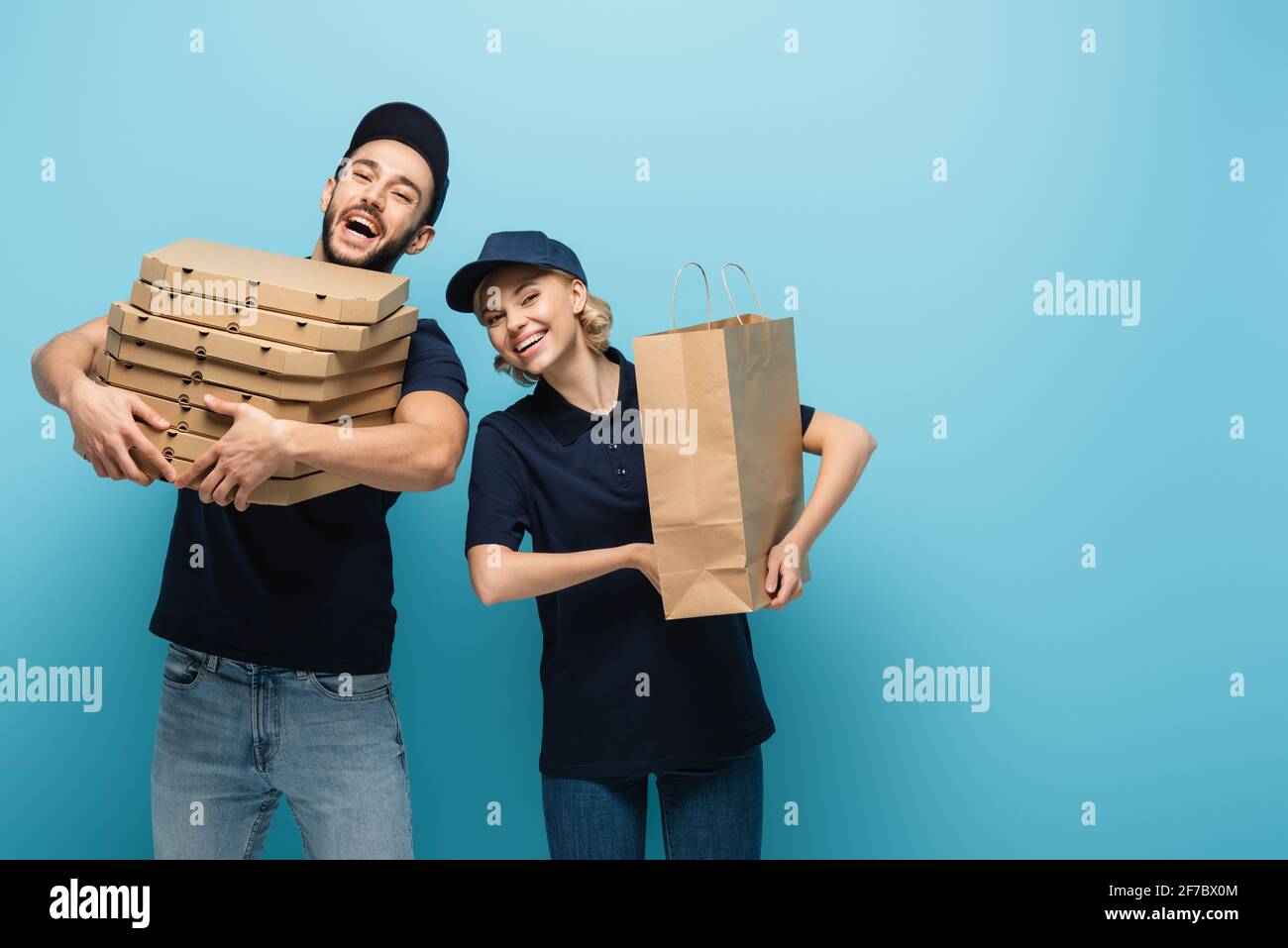 arabian delivery man laughing while holding pizza boxes near colleague ...