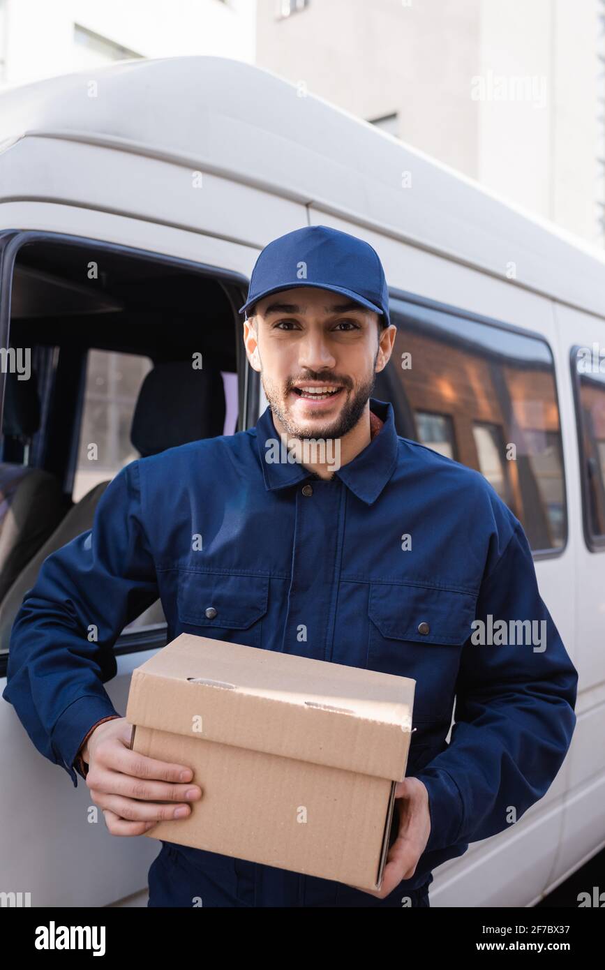 cheerful arabian postman looking at camera while holding parcel Stock ...