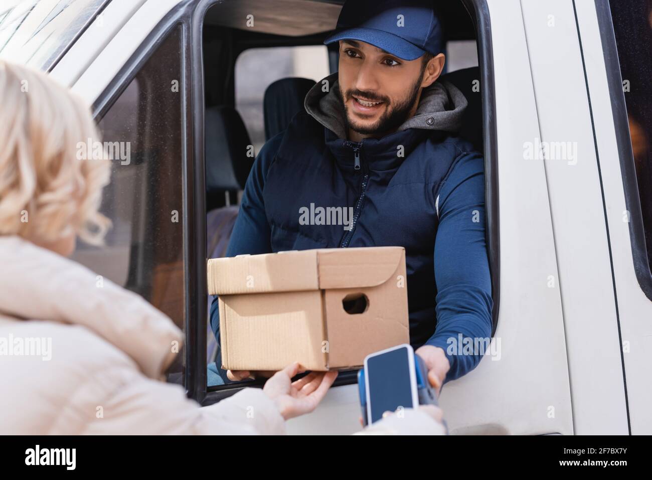 arabian postman holding box and payment terminal near woman with mobile ...