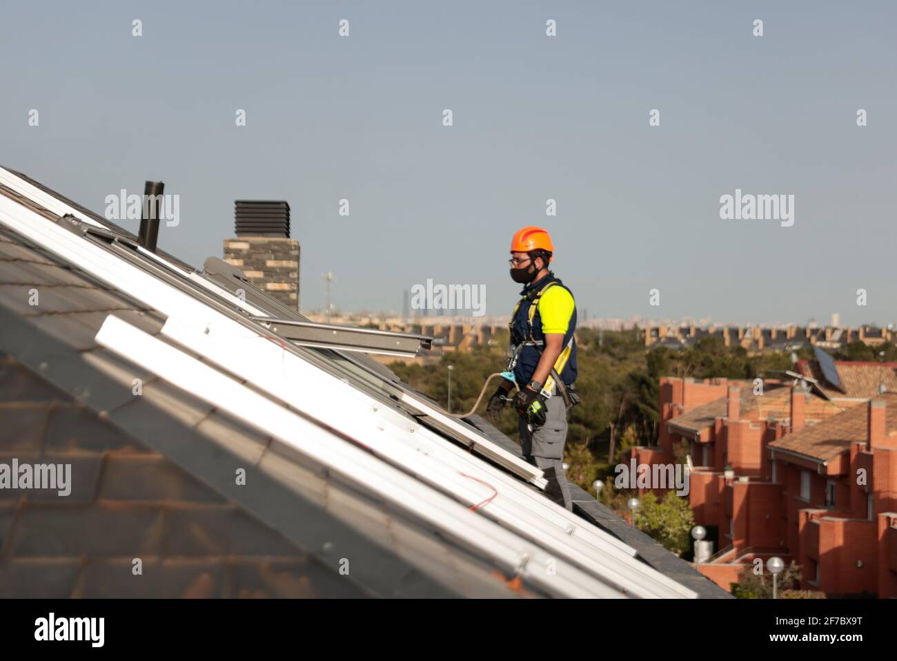 Workers wearing face masks install solar panels on a roof at a ...