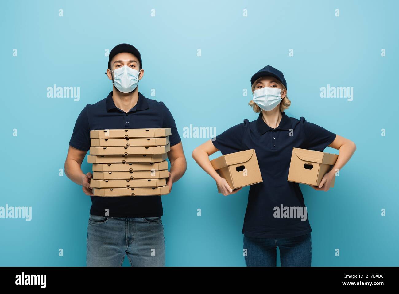 interracial couriers in protective masks holding pizza boxes and carton ...