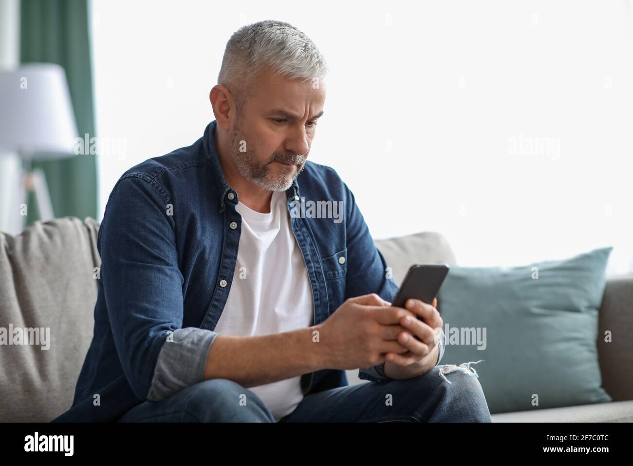 Grey-haired matured man sitting on couch, using mobile phone Stock Photo - Alamy