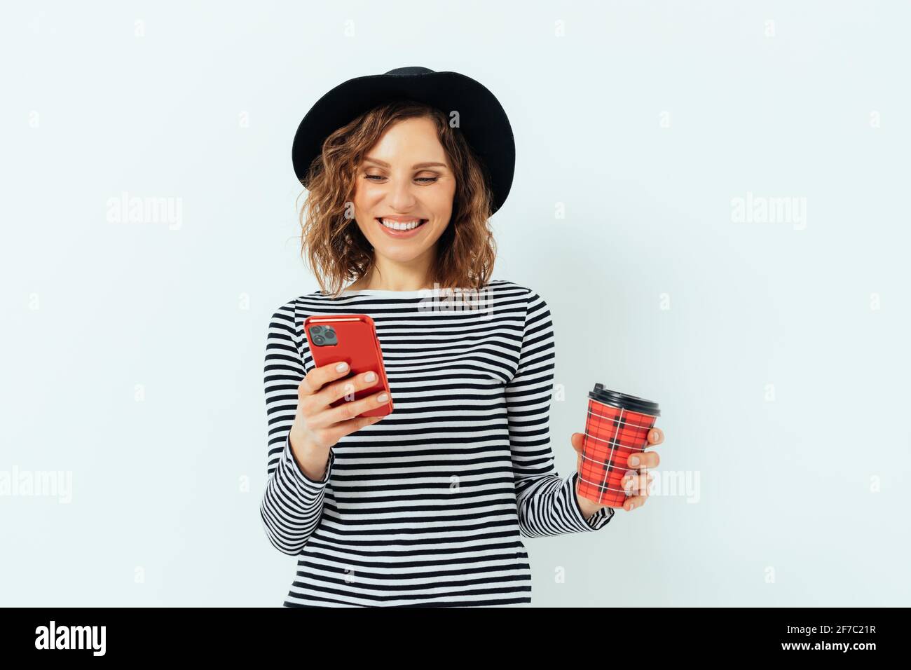 Happy young woman wearing fedora hat looking into her smart phone ...