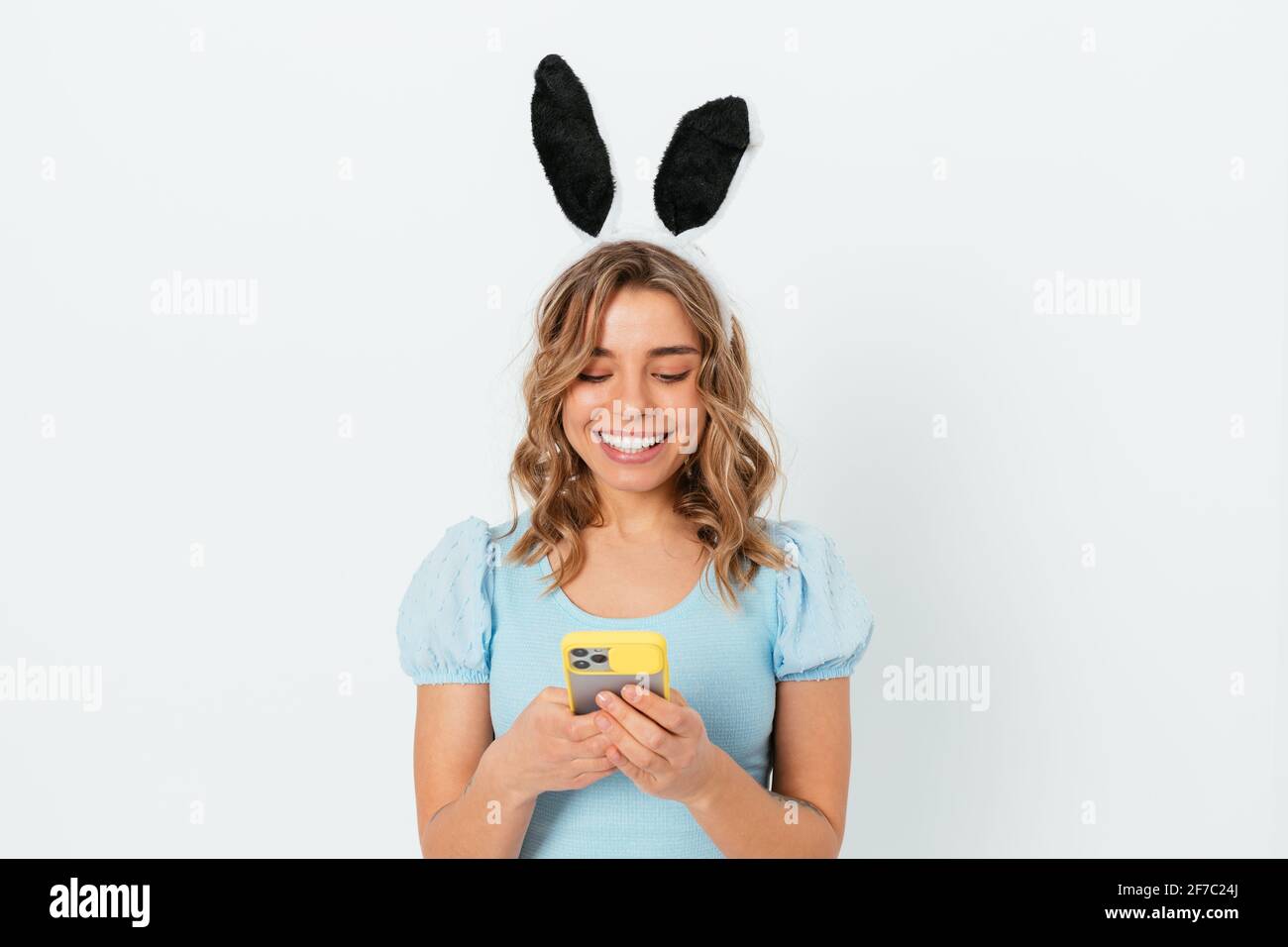 Cheerful happy young woman wearing easter bunny ears holding mobile ...